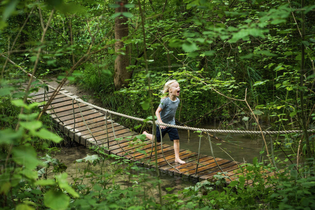 Boy running across pedestrian rope bridge in forest - Stock Photo ...