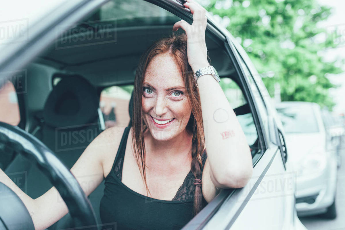 Portrait of young woman with long red hair and freckles at car window ...