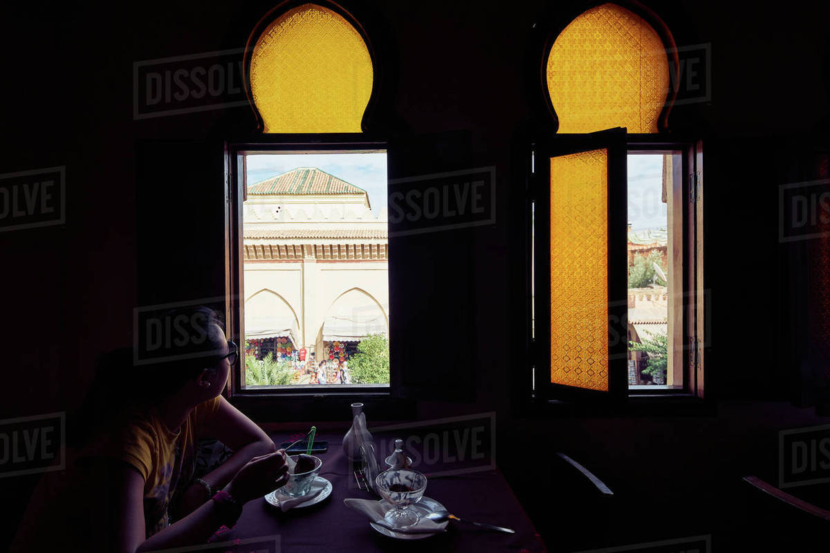 Woman eating dessert and looking through restaurant window, Marrakech ...