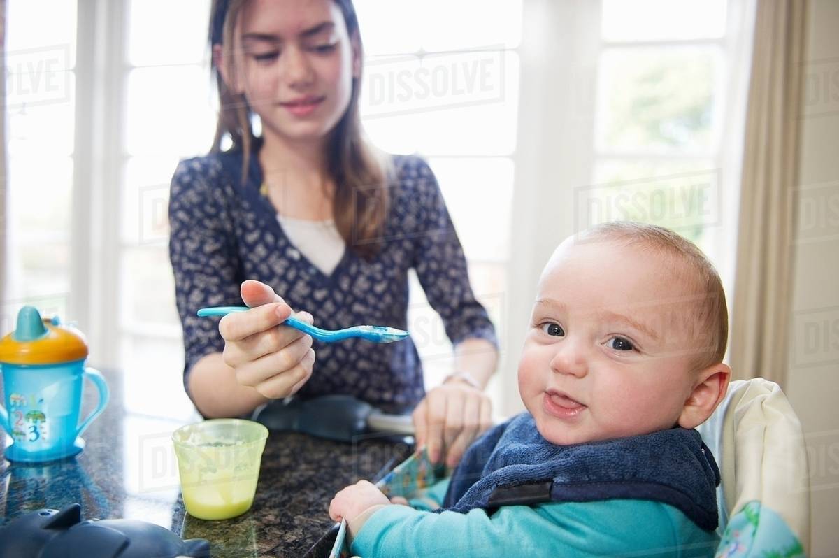 Girl feeding baby brother at table - Royalty-free Stock Photo | Dissolve