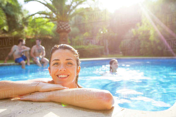 Woman in swimming pool resting on poolside looking at camera smiling ...