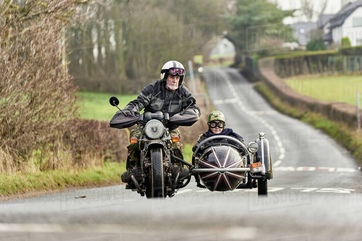 Senior man and grandson riding motorcycle and sidecar on rural road ...