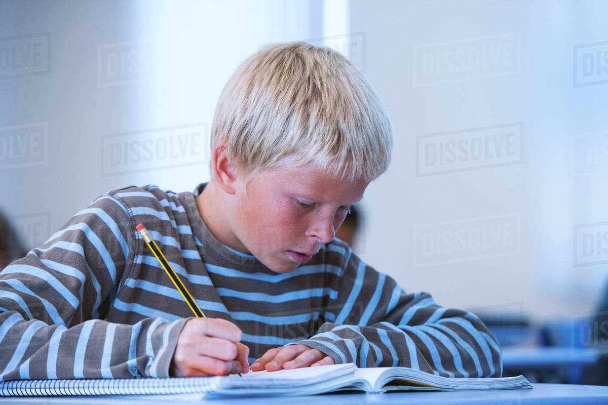 Boy in classroom, sitting at desk, doing classwork - Royalty-free Stock ...