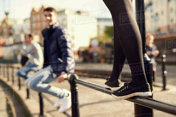 Young man sitting on railing, young girl walking along railing next to ...