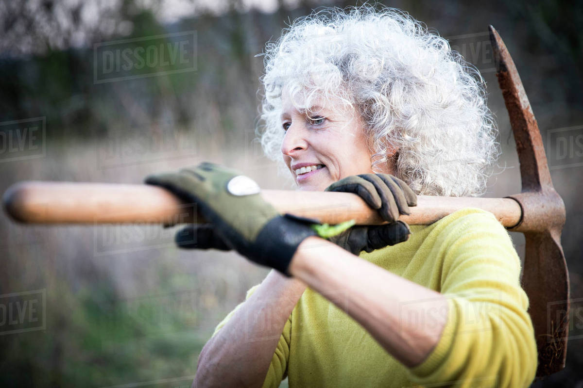 Mature woman with grey hair carrying pick axe over her shoulder in ...