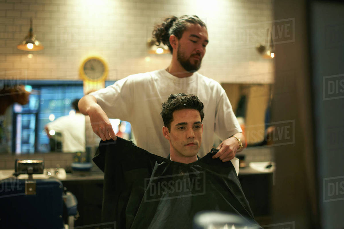 Barber putting gown onto male customer in barber shop - Royalty-free ...