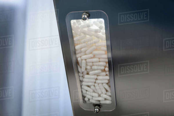 Capsules in hopper in pharmaceutical factory - Stock Photo - Dissolve