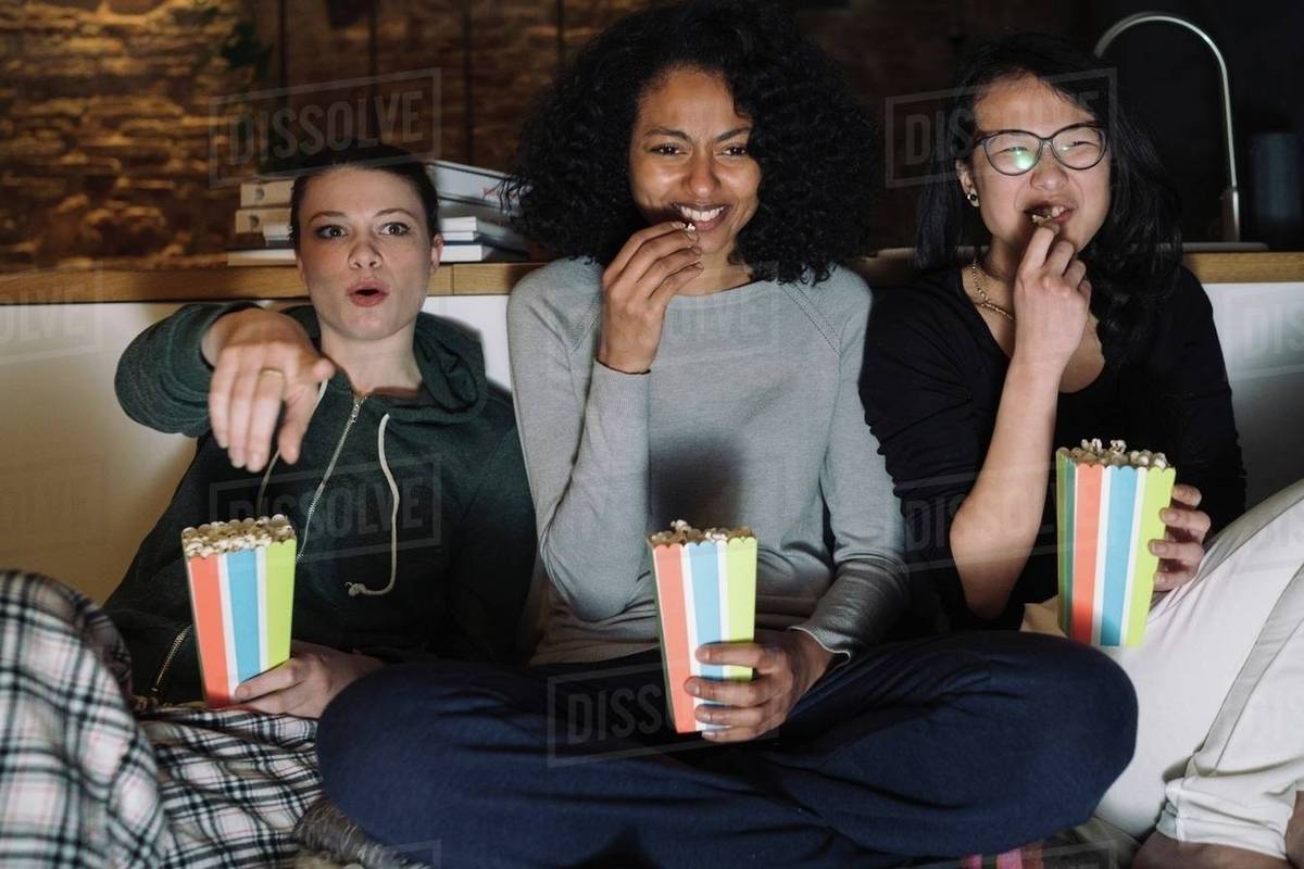 Friends on sofa eating popcorn - Stock Photo - Dissolve