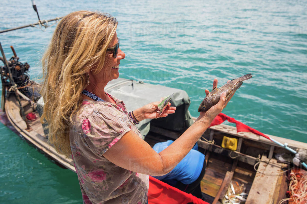 Woman holding fish by longtail fishing boat, Koh Yao Yai, Thailand ...