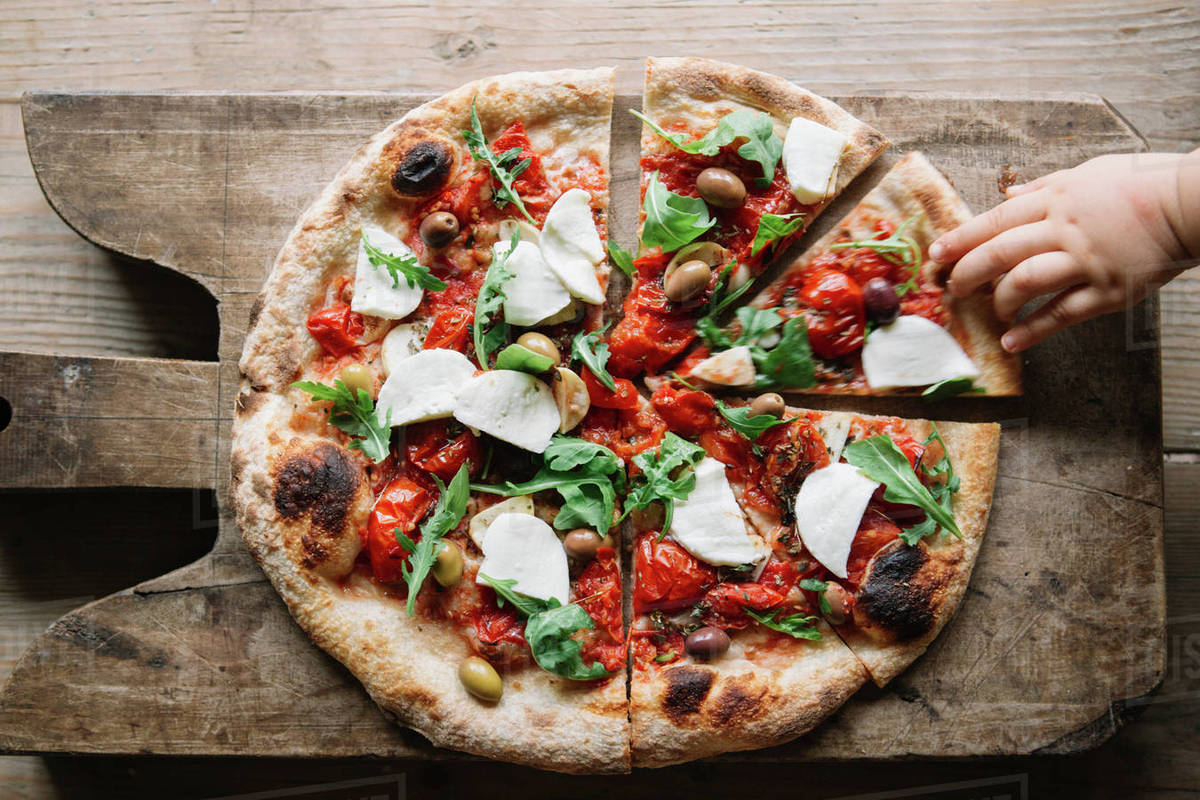 Sliced pizza on chopping board, child's hand reaching for pizza slice ...