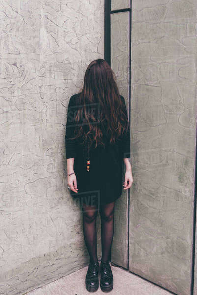 Portrait of young woman standing in corner, hair covering face ...