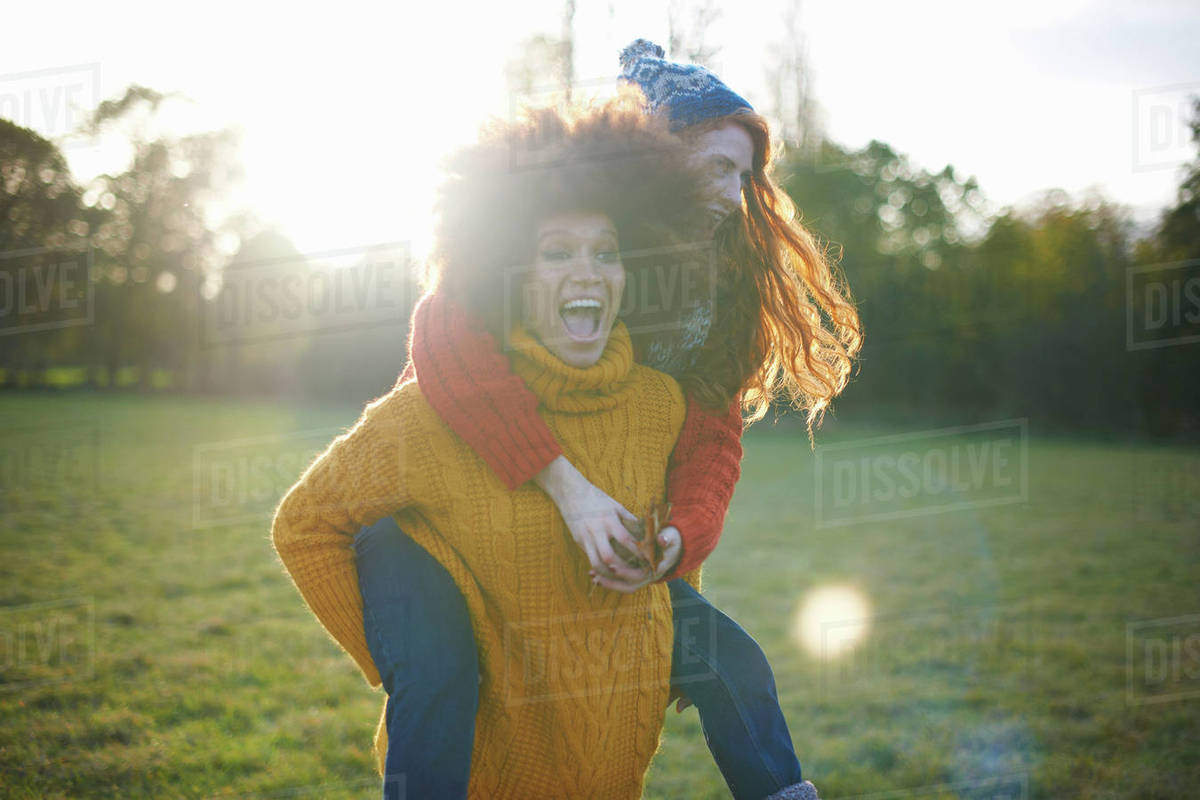 Two young women, in rural setting, young woman giving friend piggyback ...