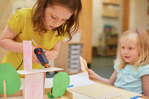 Primary schoolgirls making cardboard model at classroom desk - Royalty ...