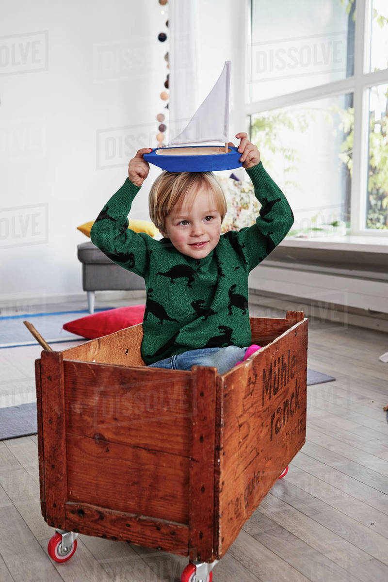 Young boy sitting in toy box, holding toy boat on head - Royalty-free ...