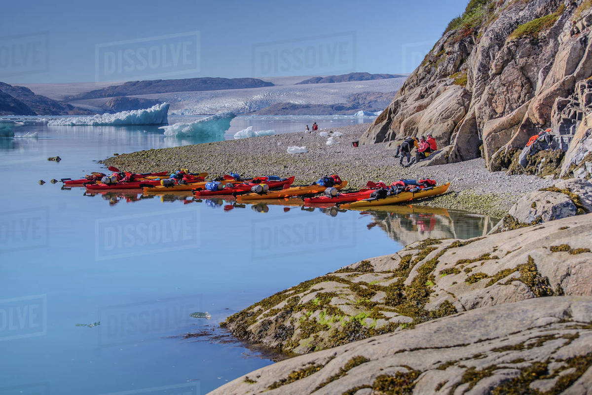 Adventure tourists on fjord beach with rows of kayaks, Narsaq ...