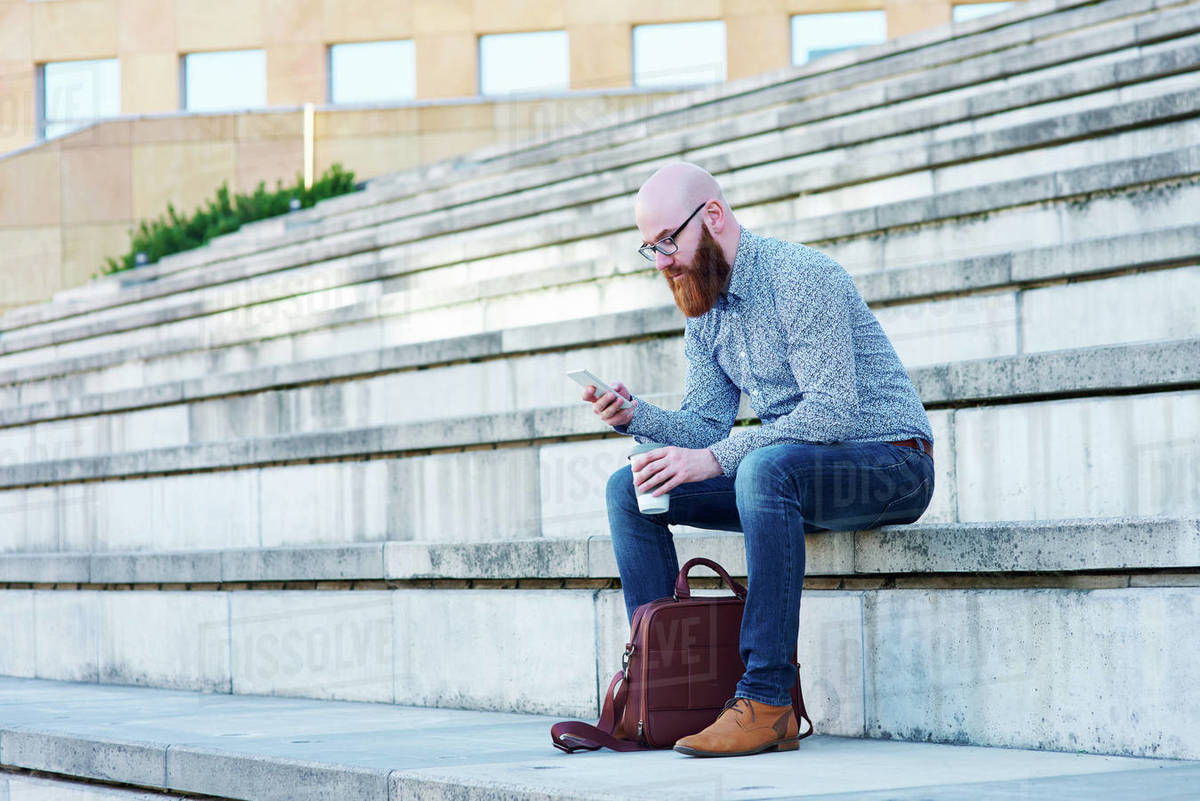 Bearded man sitting on step using smartphone - Stock Photo - Dissolve