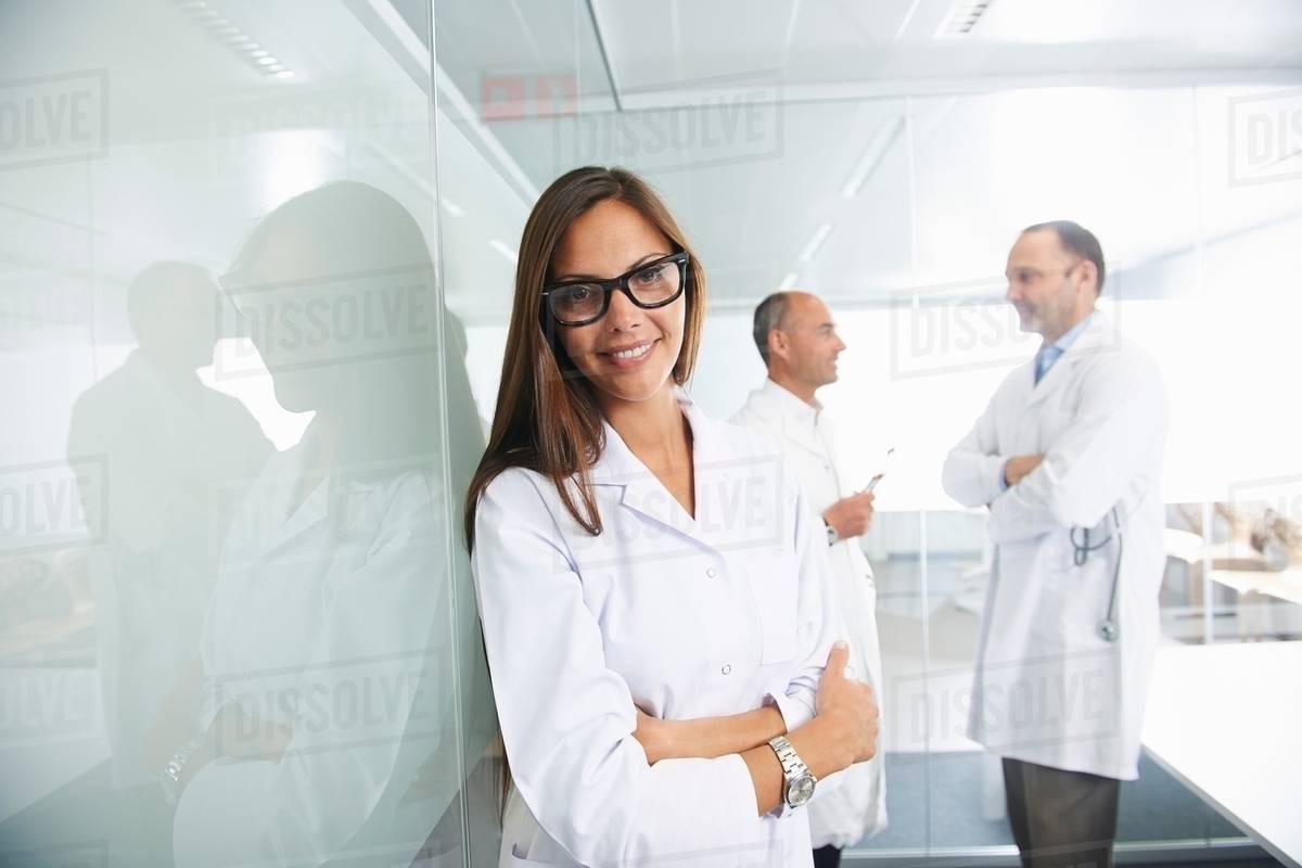 Female doctor by reflective wall, colleagues in background - Stock ...