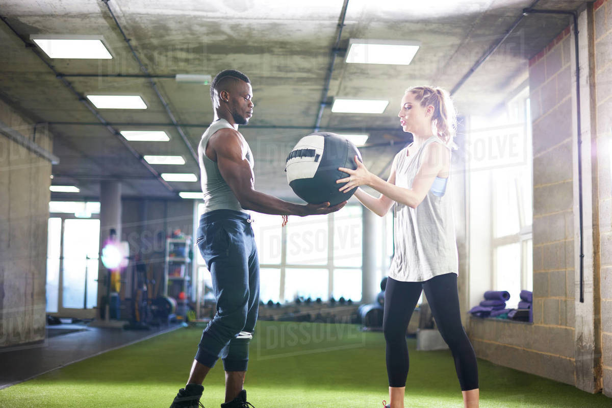 Trainer handing over medicine ball to female client in gym - Stock ...