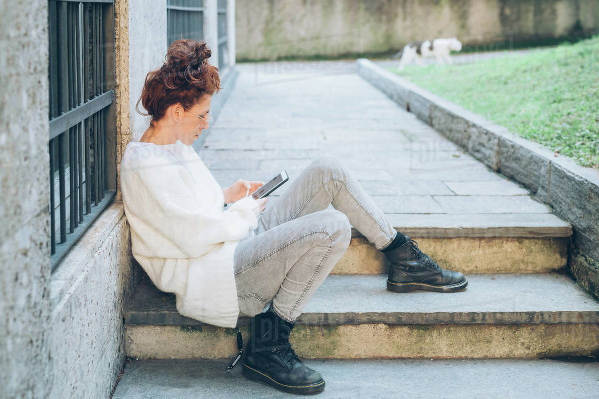 Woman using cellphone on step by building - Stock Photo - Dissolve