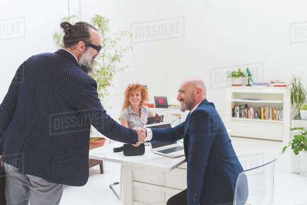 Businessman and client shaking hands at office desk - Royalty-free ...