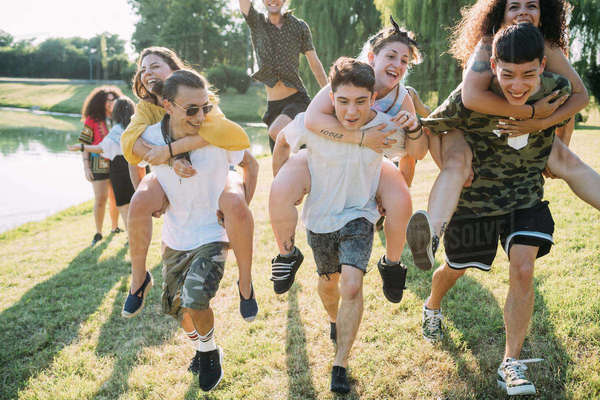 Group of friends piggyback racing in park - Stock Photo - Dissolve