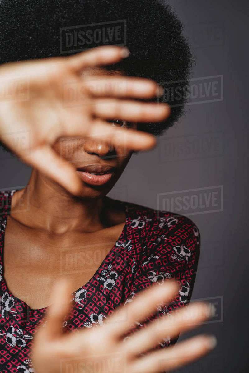 Young woman with afro hair covering face with hands, grey background ...
