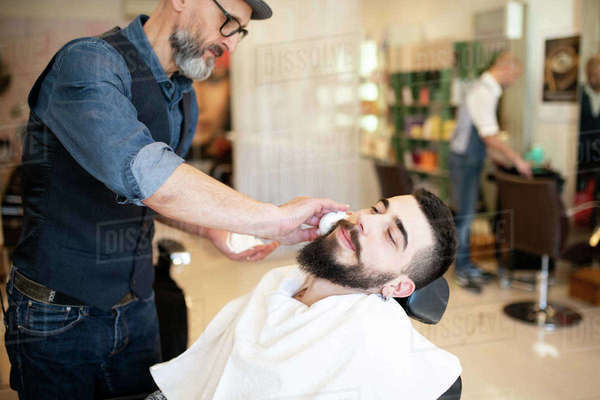 Hairdresser preparing to shave customer's beard in barber shop ...