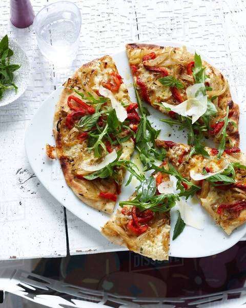 Plate of sliced wholemeal pizza with herbs, vegetable and parmesan ...