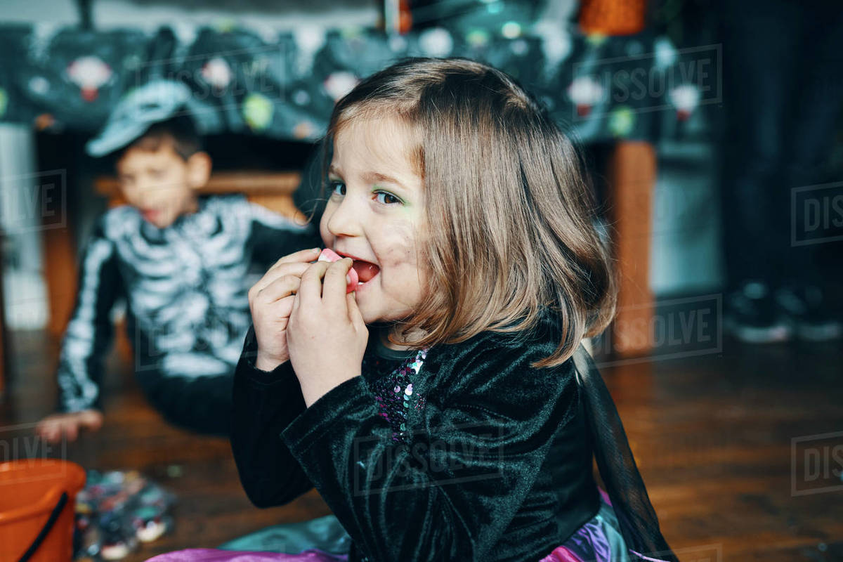 A girl smiling and eating sweets with a boy dressed as a skeleton in ...