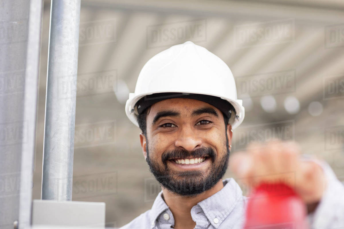 A focused man wearing a white hard hat is looking intently at something ...