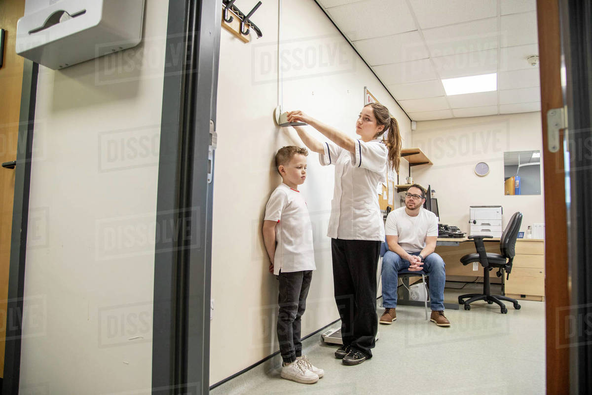 Child being measured during a medical check-up as father observes ...