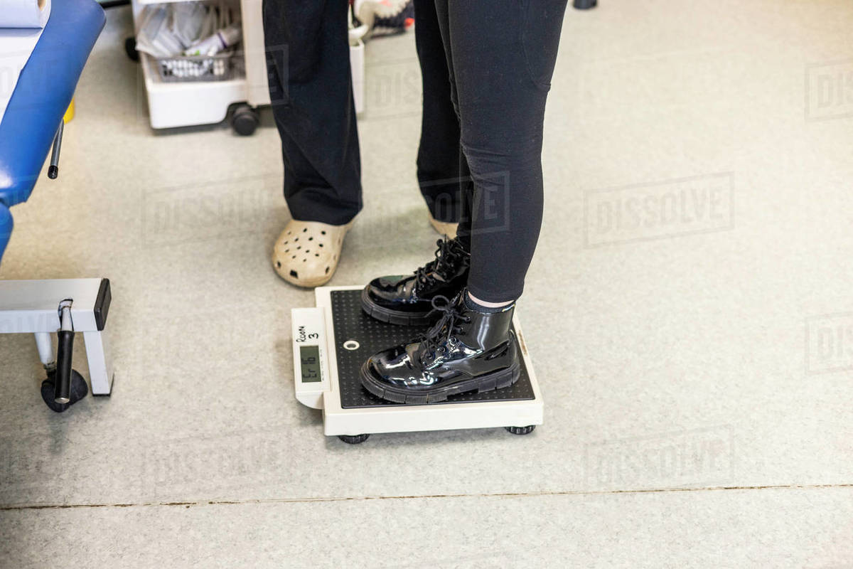 Medical professional palpating patient's back while on a scale in a ...