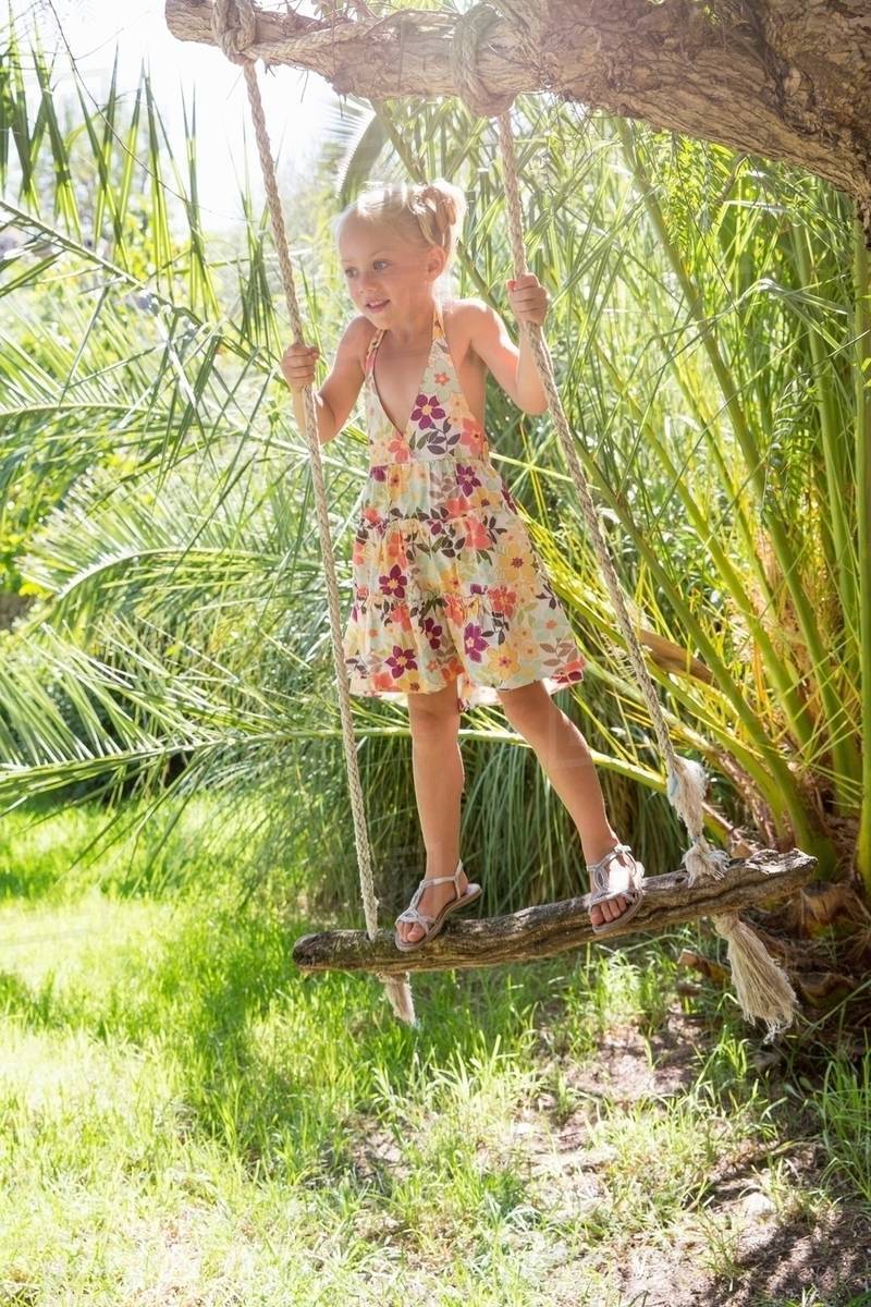 Girl standing swinging on tree swing in garden - Stock Photo - Dissolve