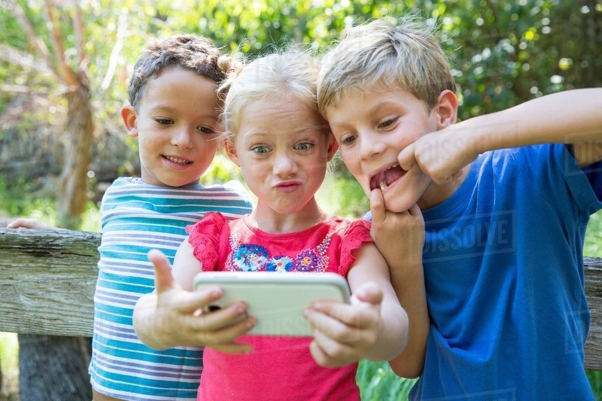 Three children in garden taking selfie on smartphone - Royalty-free ...