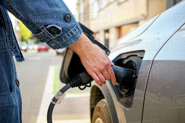 Close-up of a person's hand inserting a charging plug into an electric ...