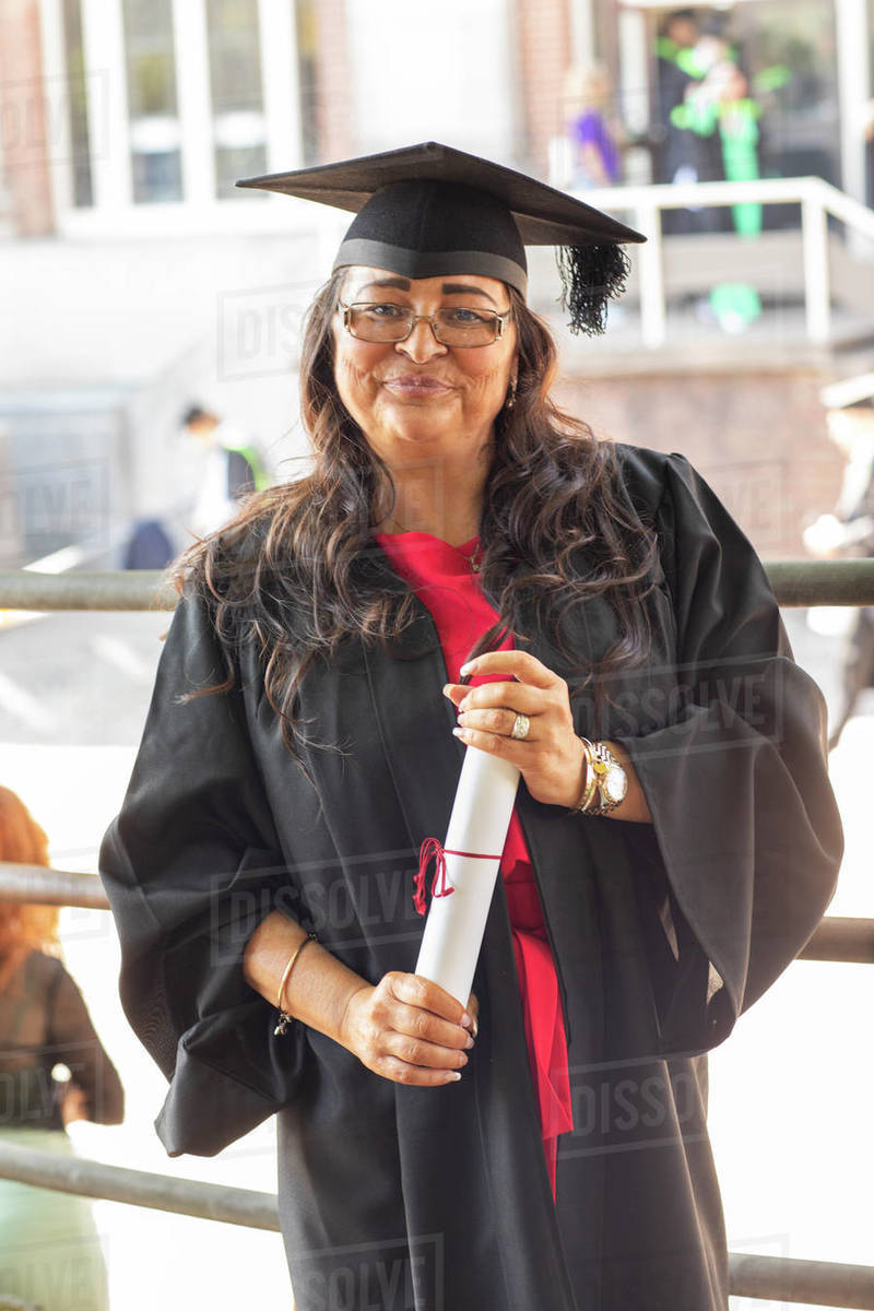 Smiling woman in graduation gown and cap holding a diploma with a red ...