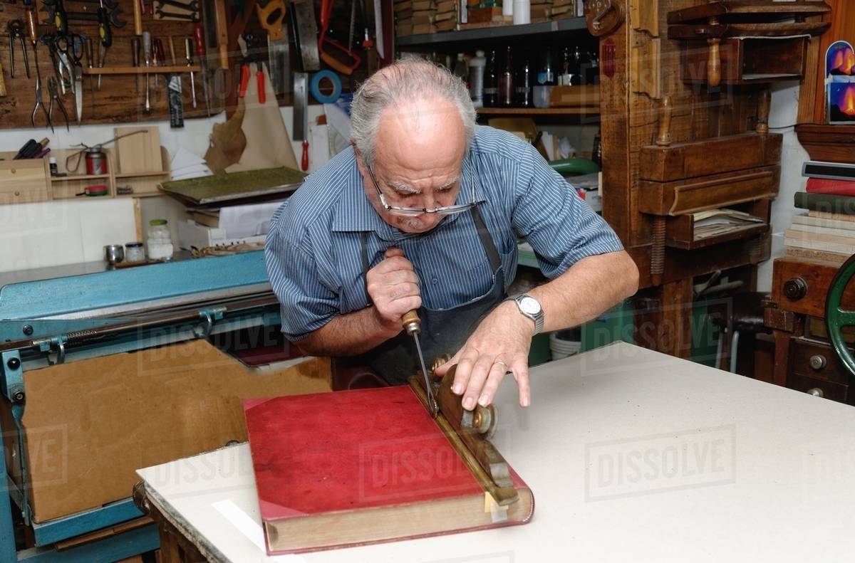 Senior man restoring book in traditional bookbinding workshop - Royalty ...