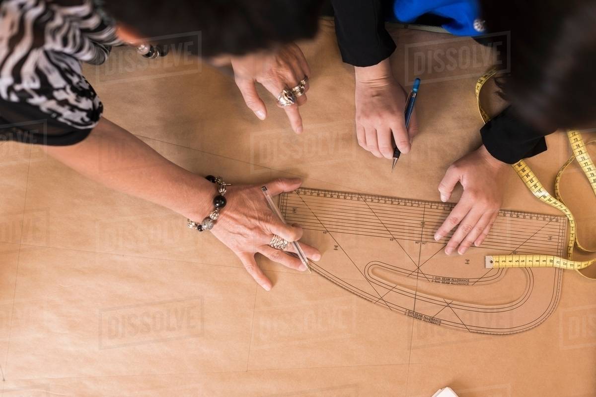 Overhead view of seamstresses hands using curved ruler on dressmakers ...