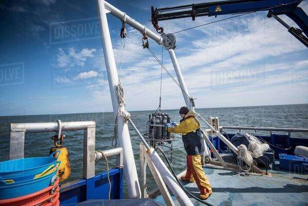 Scientist lowering sea water sampling experiment into sea on research ...