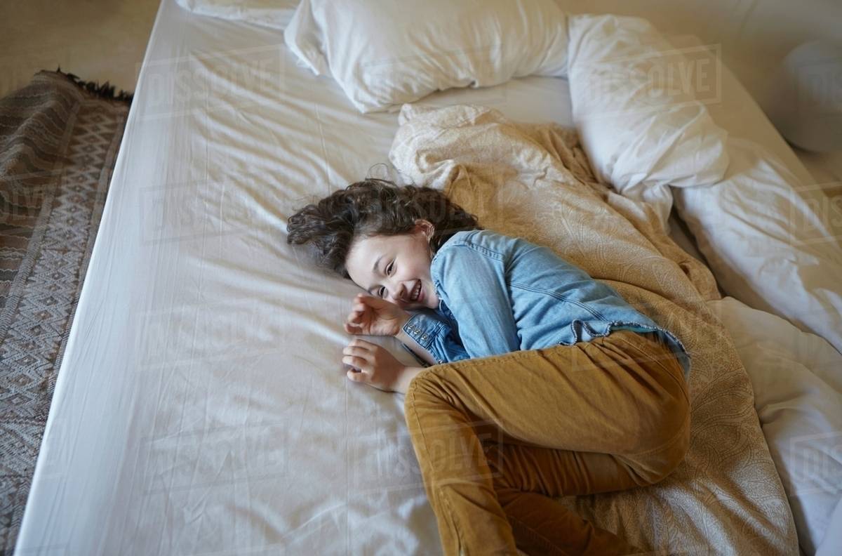 Giggling young girl curled up on bed - Stock Photo - Dissolve