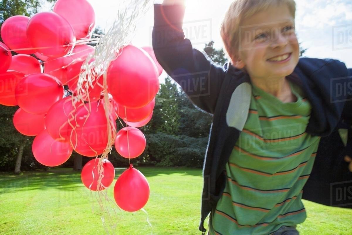 Boy carrying bunch of balloons outdoors - Stock Photo - Dissolve