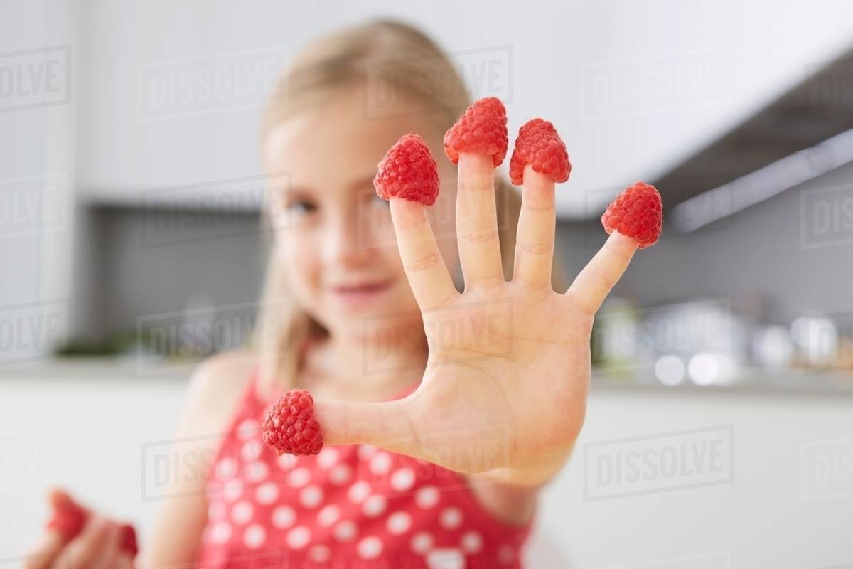 Girl putting raspberries on fingers - Royalty-free Stock Photo | Dissolve