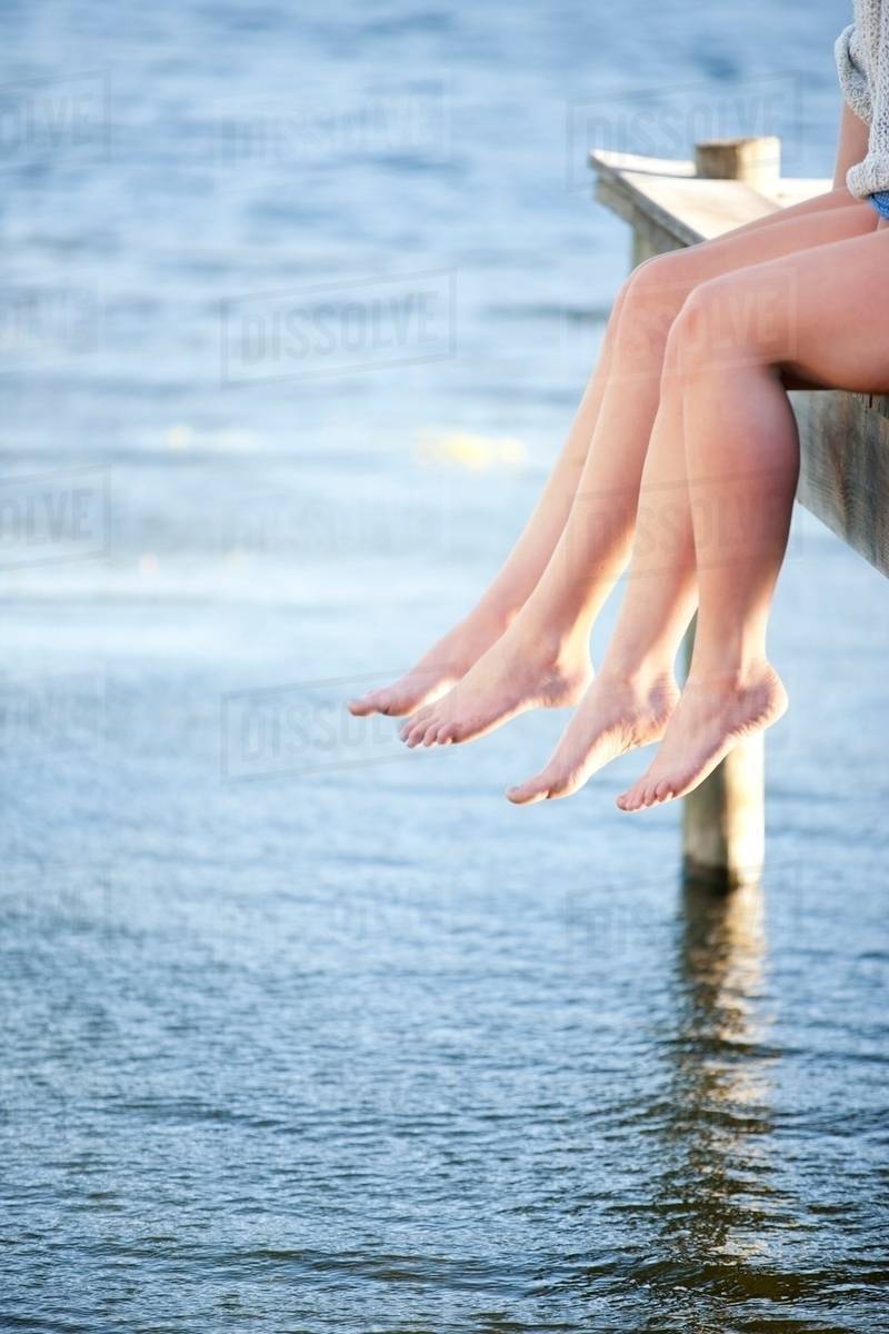 Two pairs of female legs dangling from pier - Royalty-free Stock Photo ...