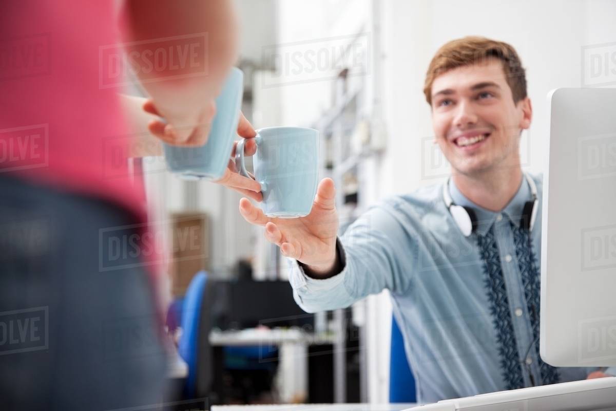 Woman giving young man coffee in office - Stock Photo - Dissolve