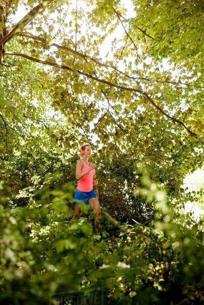 Young woman running through woods - Stock Photo - Dissolve