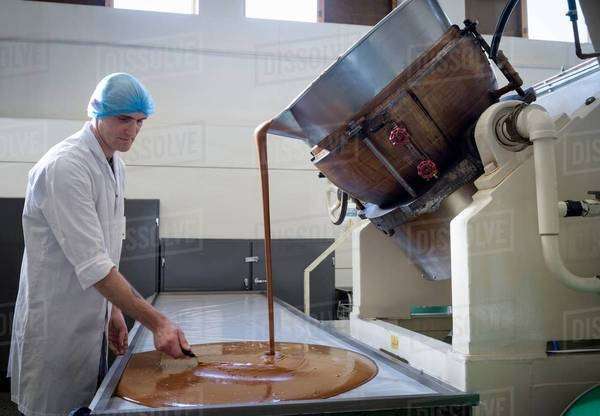 Worker spreading confectionery fudge poured in chocolate factory ...