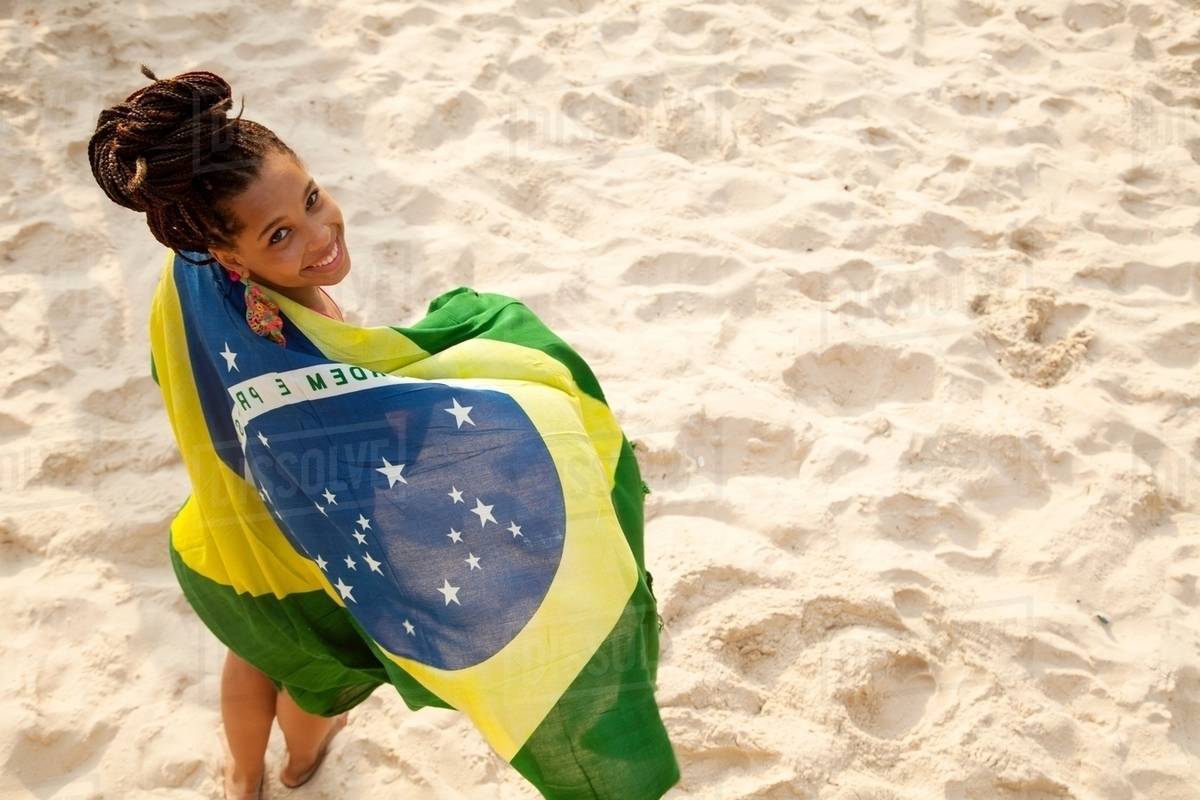 Overhead portrait of young woman wrapped in Brazilian flag, Ipanema ...