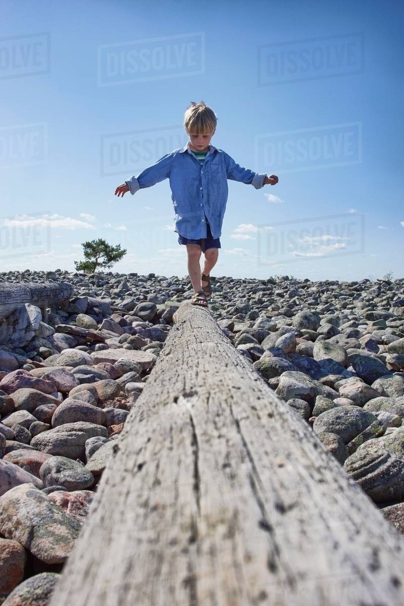 Boy balancing on log on beach - Royalty-free Stock Photo | Dissolve