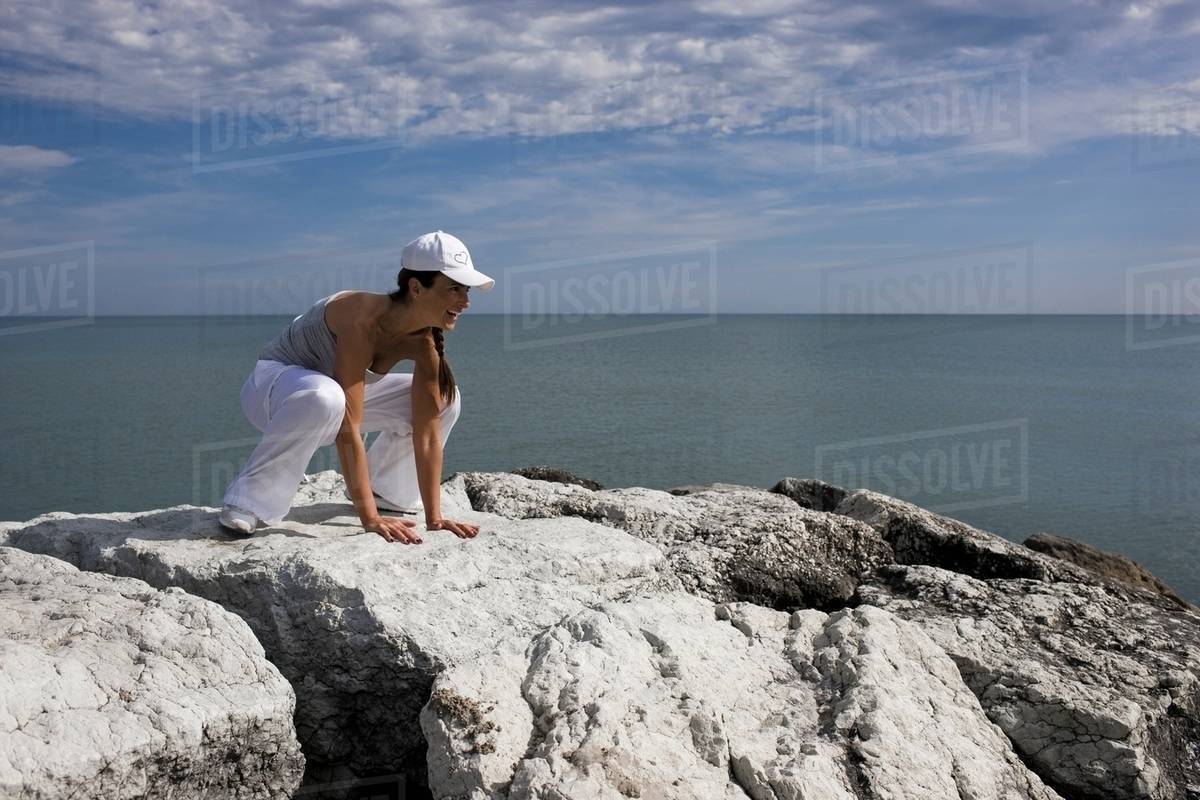 Woman hunkering down on rocks - Royalty-free Stock Photo | Dissolve