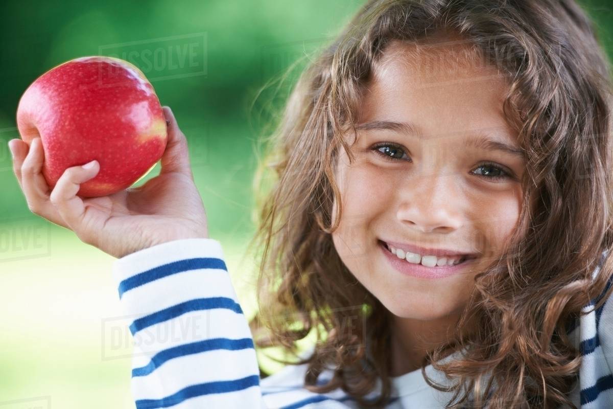 Smiling girl holding an apple - Stock Photo - Dissolve